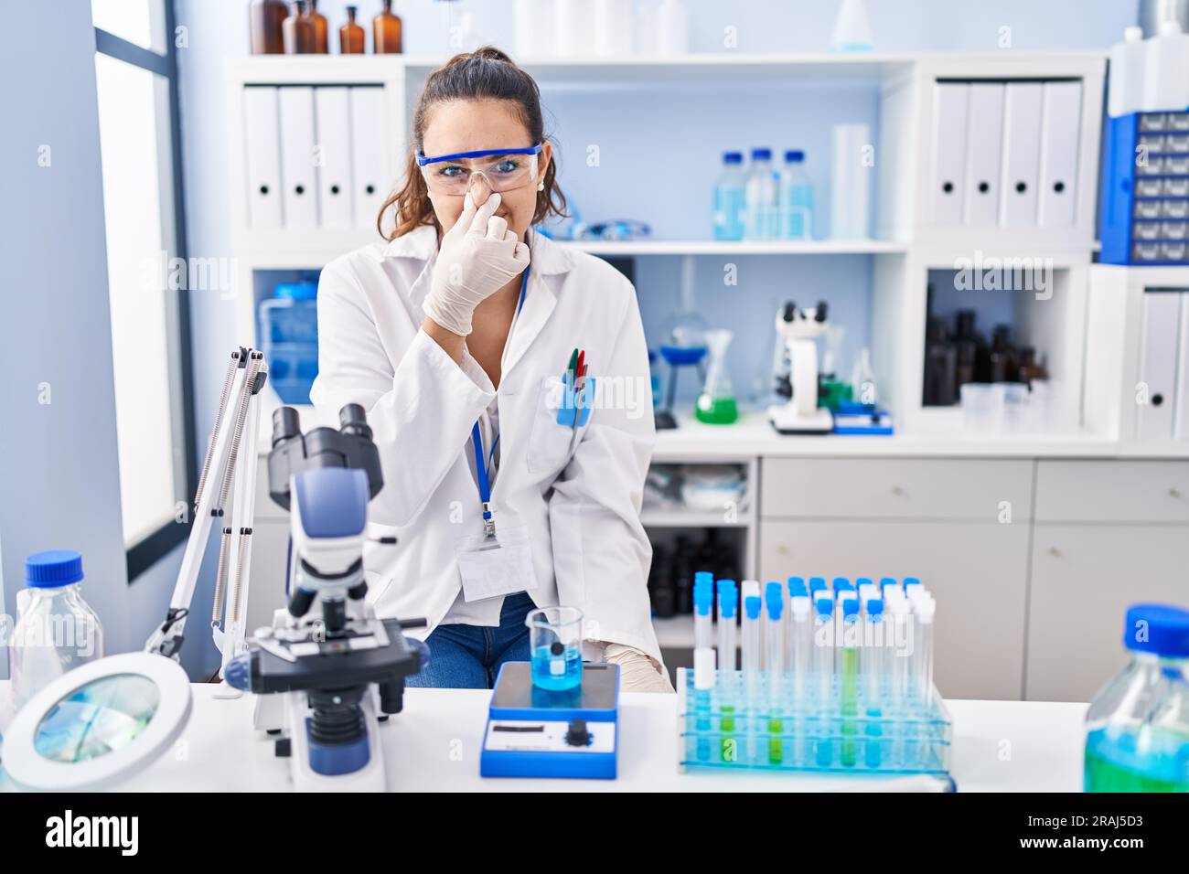 Young hispanic woman working at scientist laboratory smelling something ...