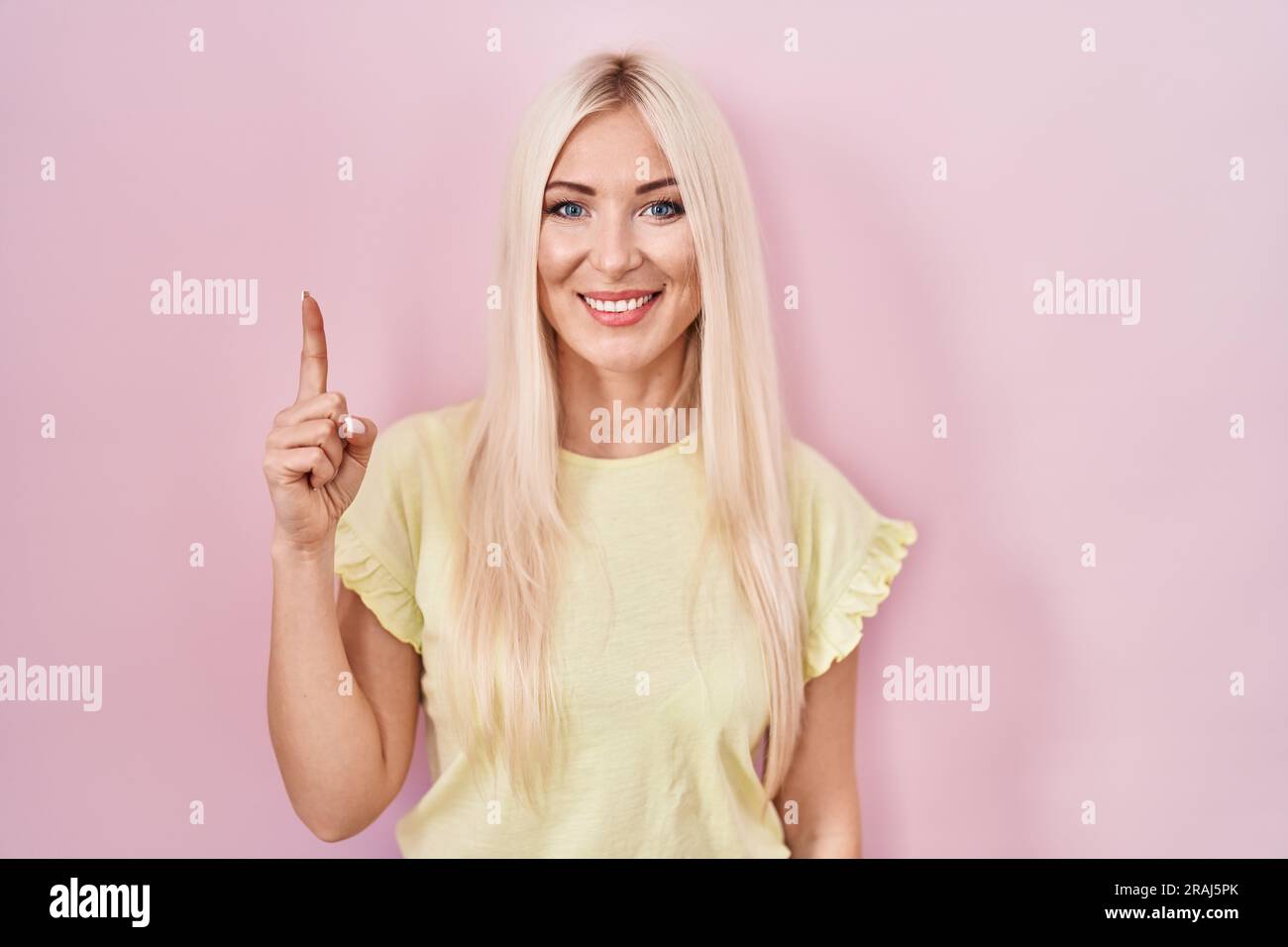 Caucasian woman standing over pink background showing and pointing up ...