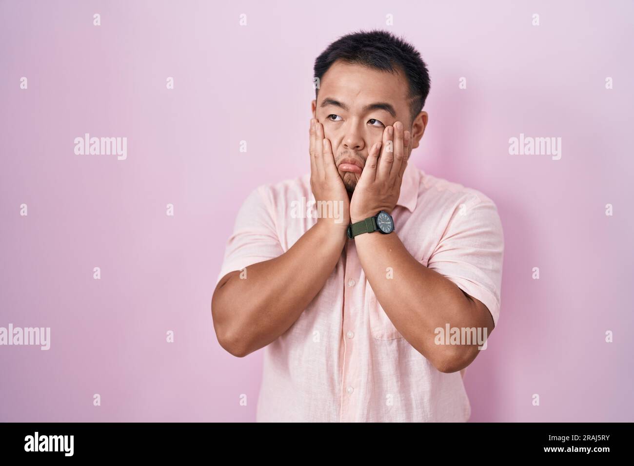Chinese young man standing over pink background tired hands covering ...