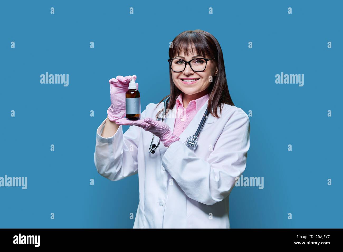 Woman doctor showing glass liquid medicine bottle, blue studio ...