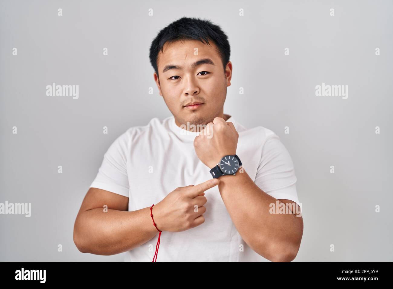Young chinese man standing over white background in hurry pointing to ...