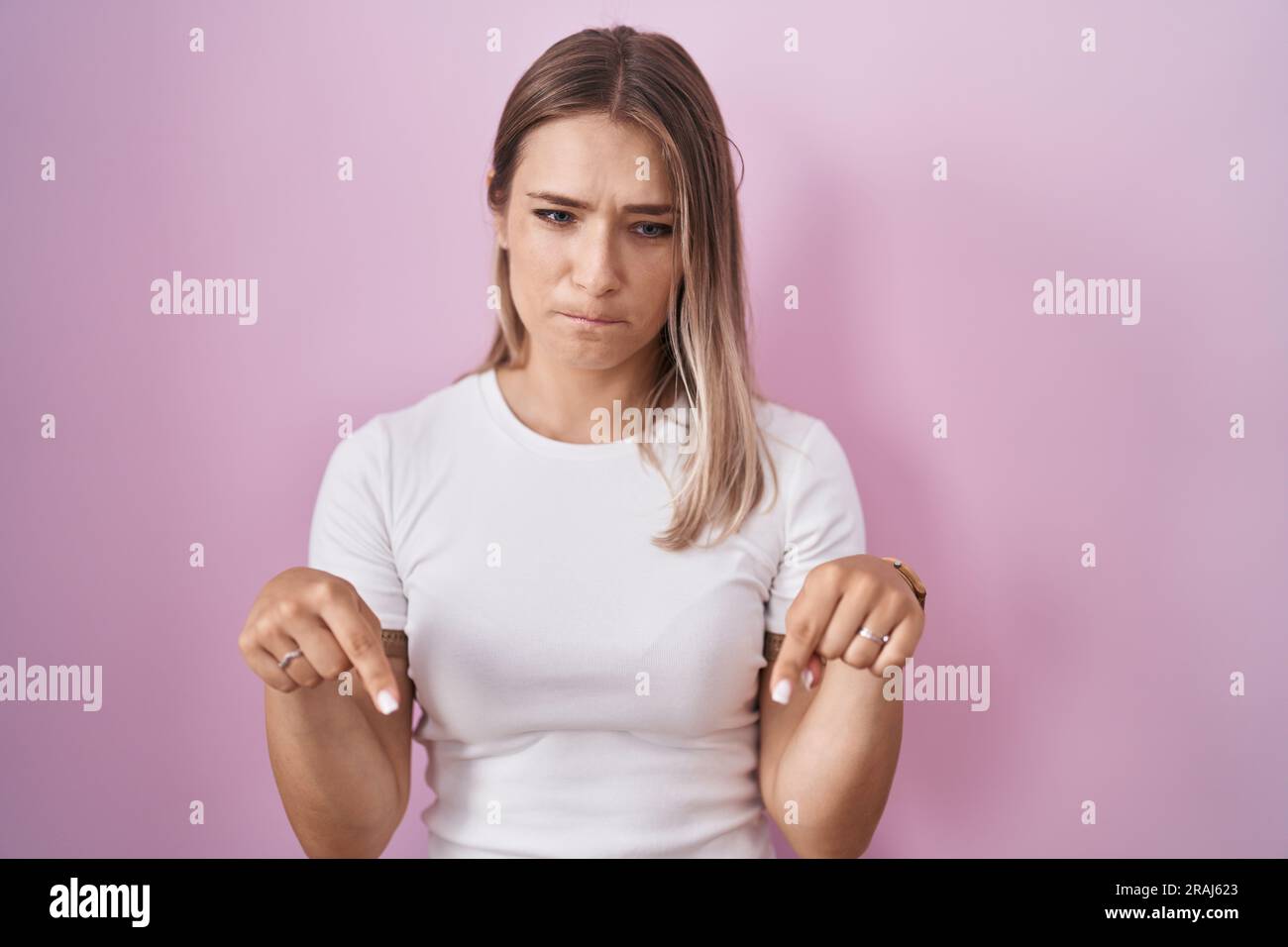 Blonde caucasian woman standing over pink background pointing down ...