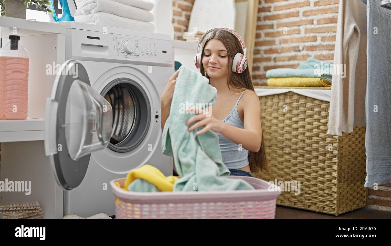 Young beautiful girl washing clothes listening to music at laundry room ...