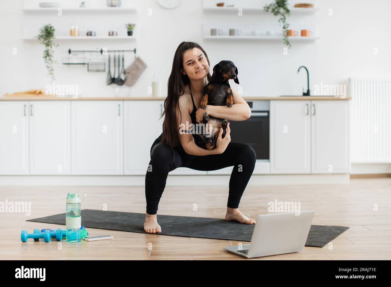 Beautiful woman in sportswear cuddling Dachshund while doing squats on ...