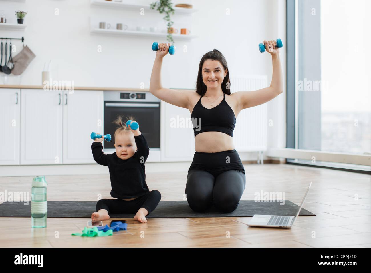 Full length view of smiling mother and infant in sportswear lifting ...