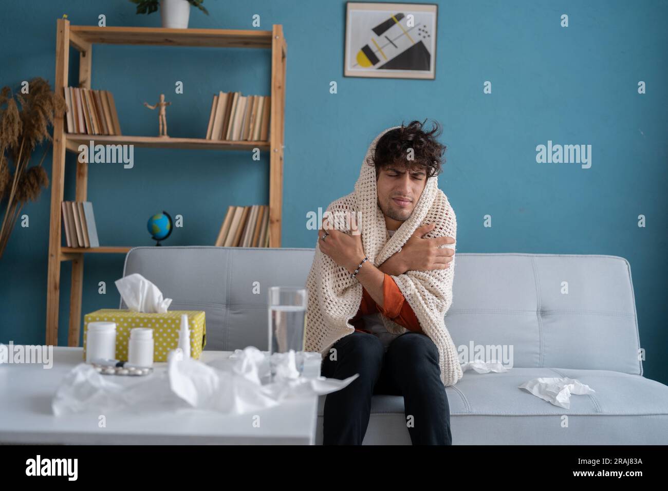 Unhappy young man wrapped in blanket suffering from symptoms of common ...