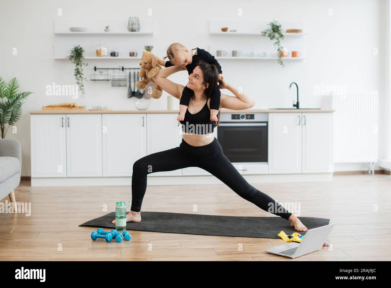 Beautiful female practising asana while holding child with cuddly bear ...