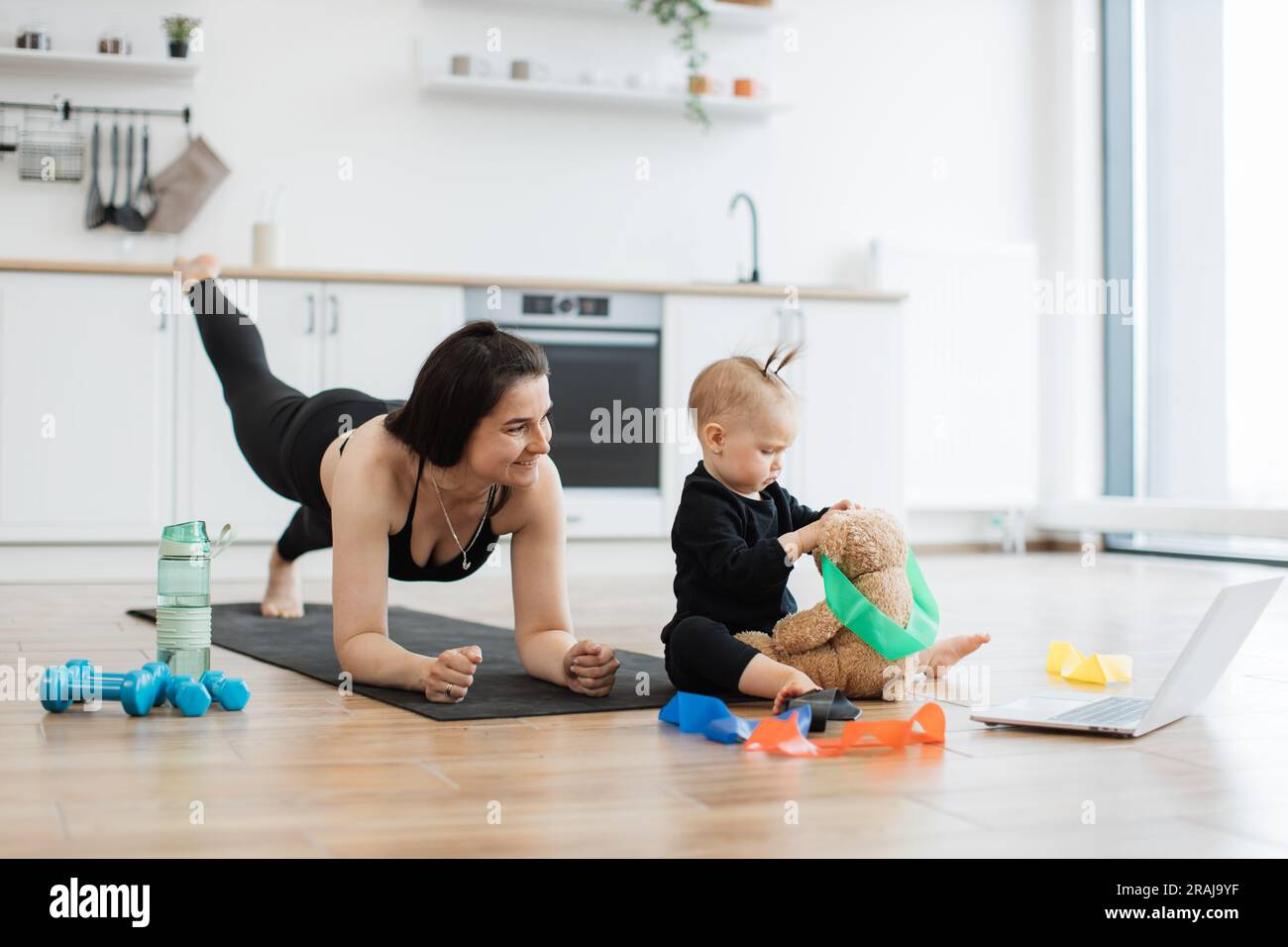 Healthy lady stretching in forearm plank while watching small baby ...
