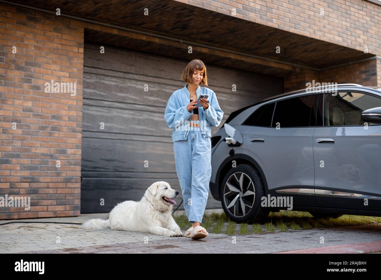 Woman charges electric car near a house Stock Photo - Alamy