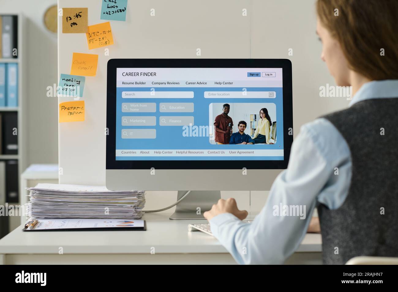 Rear view of young businesswoman sitting at table in front of computer ...
