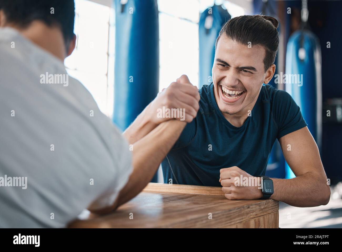 Strong, active and men arm wrestling in the gym on a table while being ...