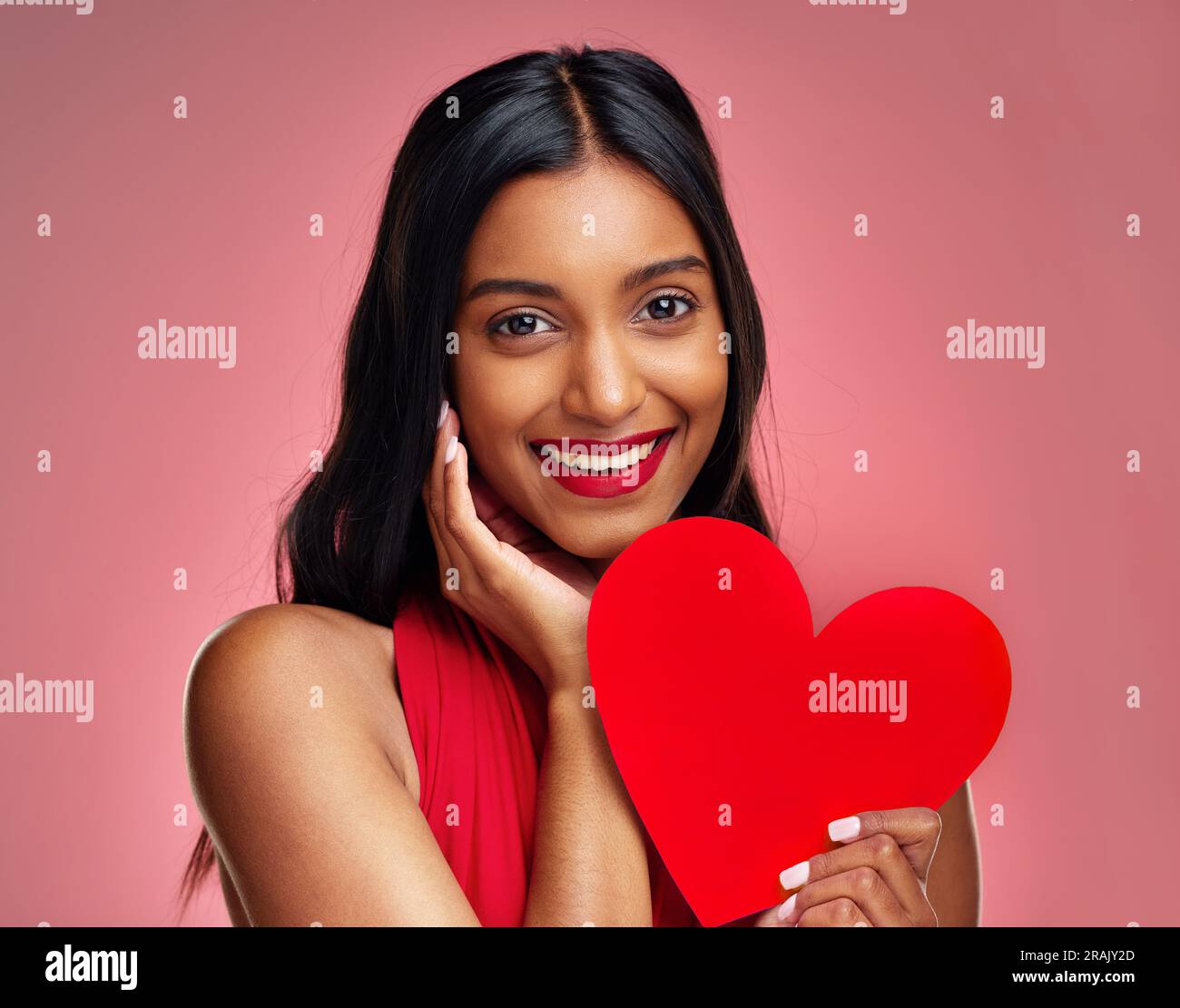 Portrait, heart and romance with a woman on a pink background in studio ...