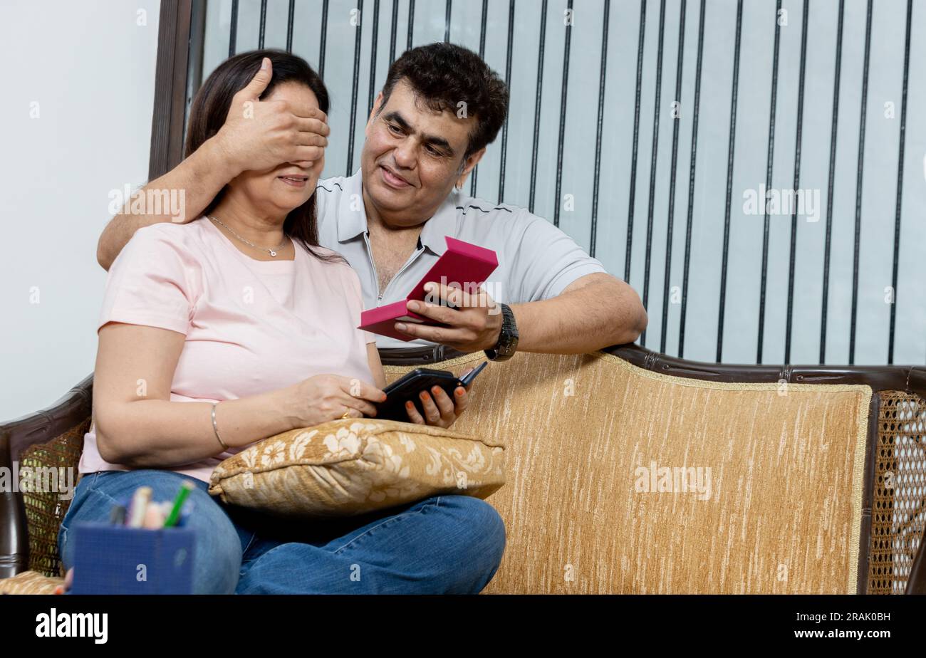 Indian husband covering his wife eyes, making birthday surprise, giving ...