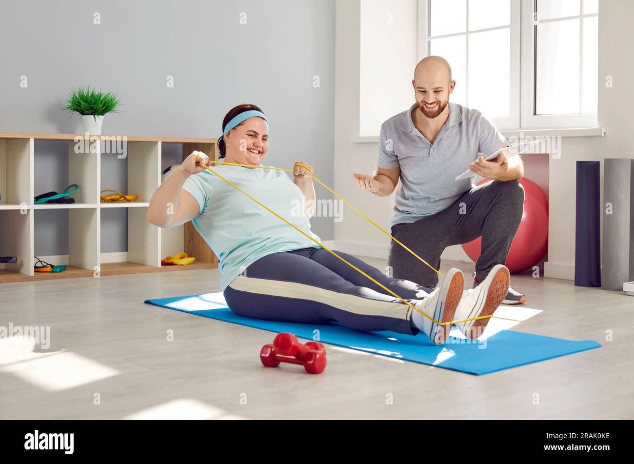 Friendly nurse helping fat woman doing stretching exercises with rubber ...