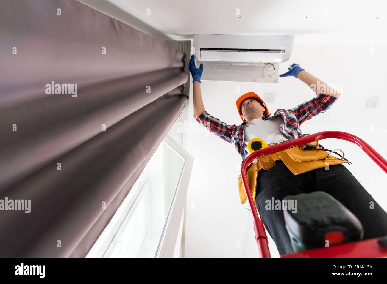 Worker installing or repairing air conditioner. Young man in uniform ...