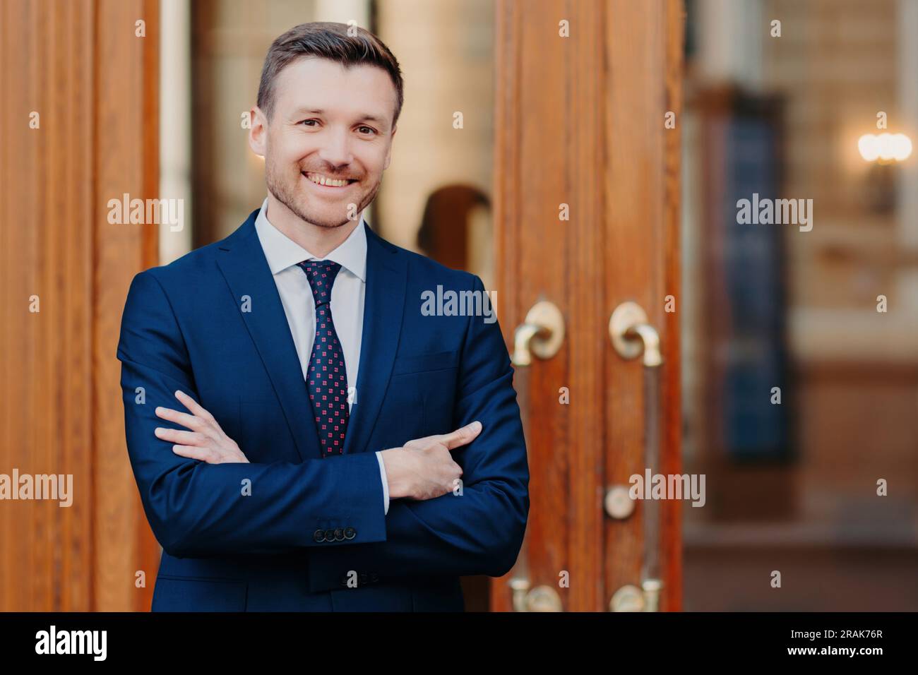 Pleased businessman, crossed hands, formal suit, by company entrance ...