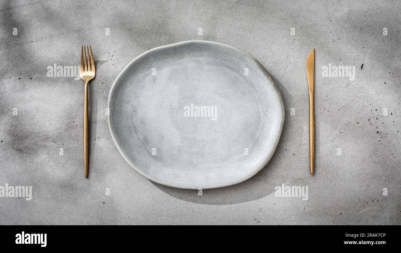 Minimal place setting in gray tones. Gray plate and gold cutlery on ...