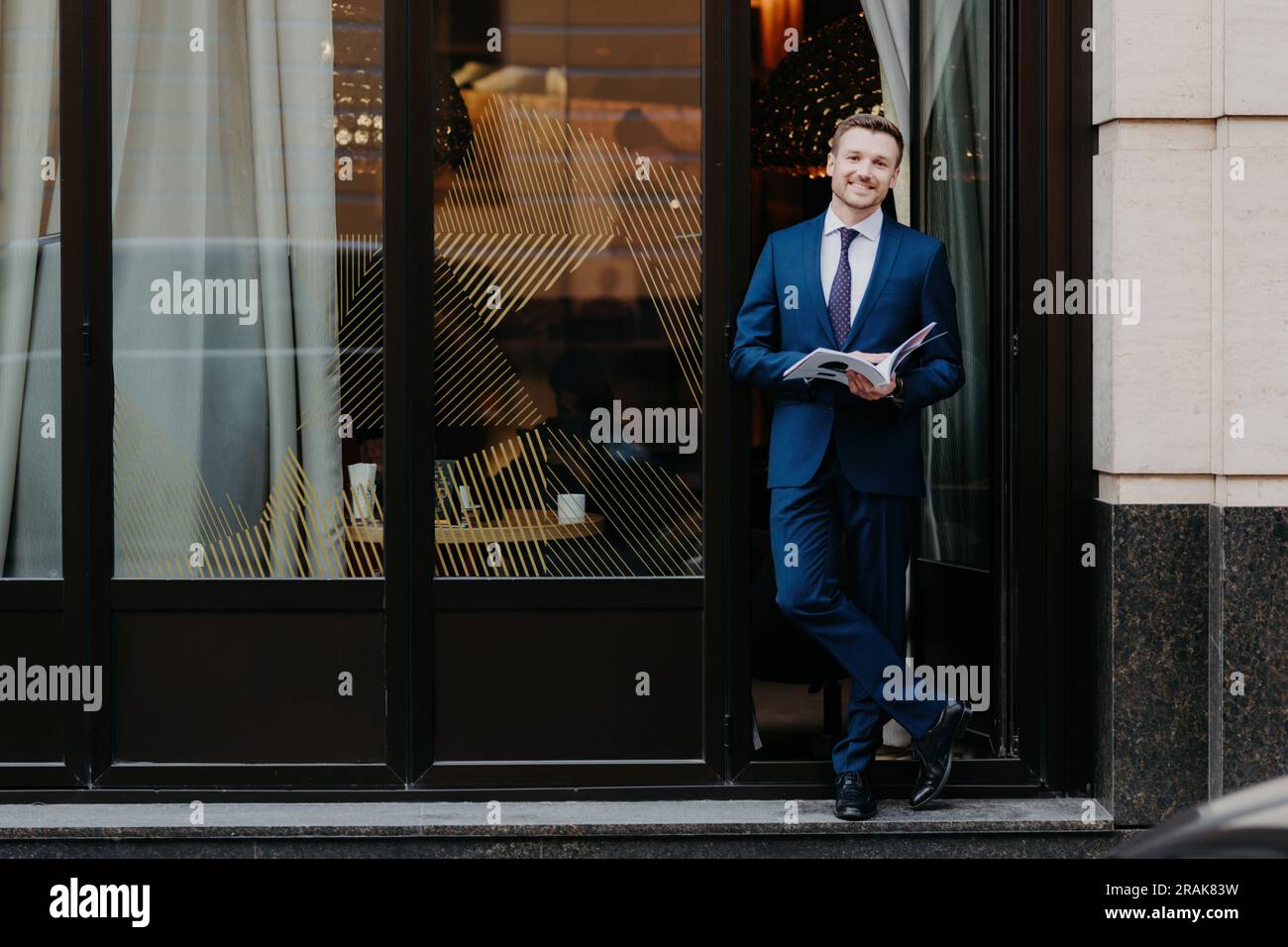 Attractive CEO in suit, crossed legs by cozy cafe, holds journal ...