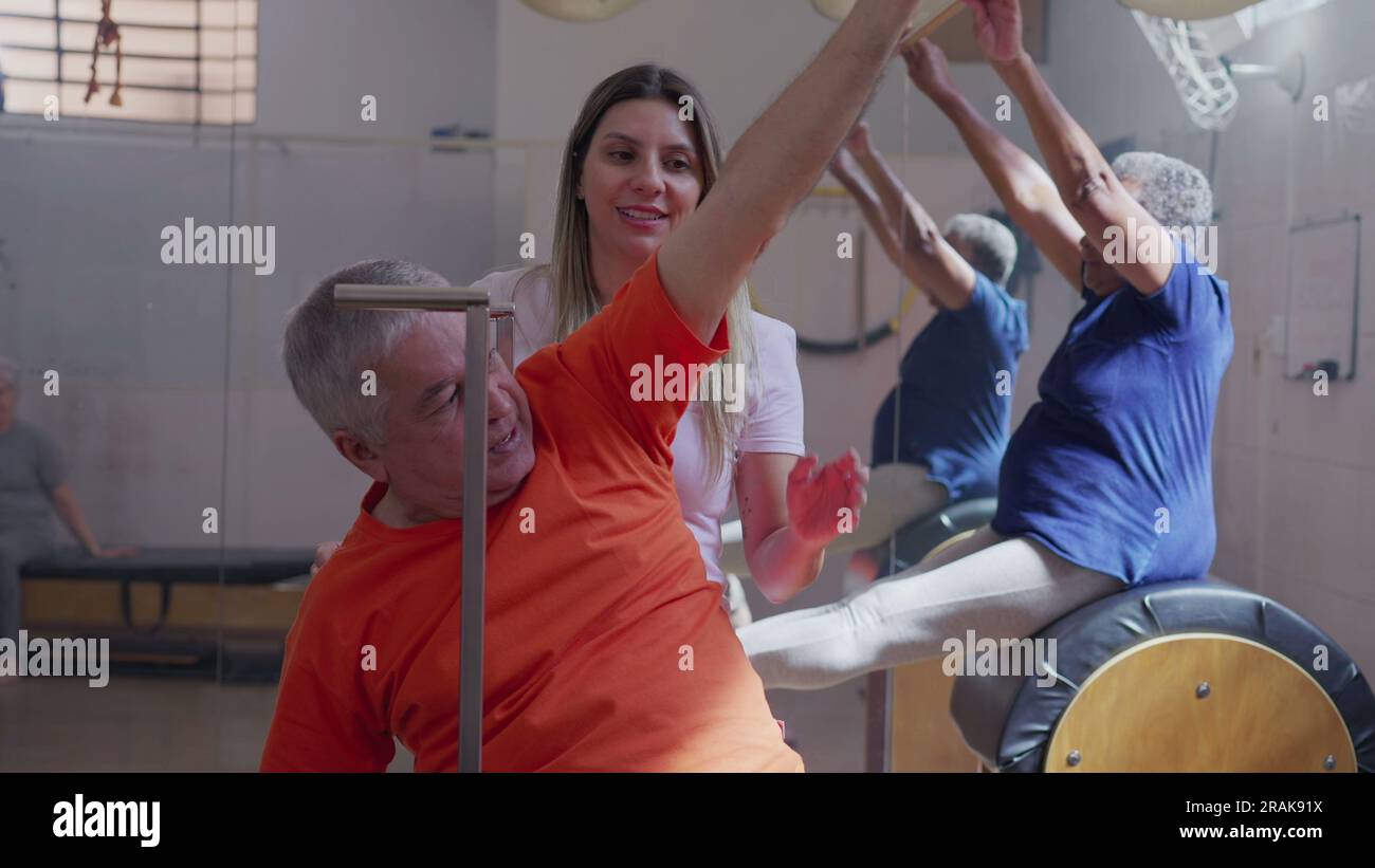 Female coach guiding senior man in group Pilates session. Old age ...