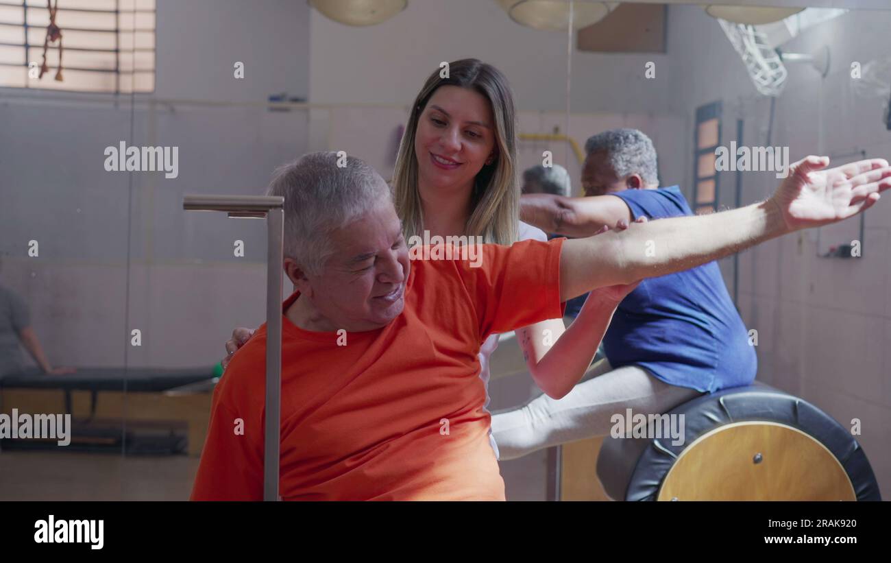 Female coach guiding senior man in group Pilates session. Old age ...