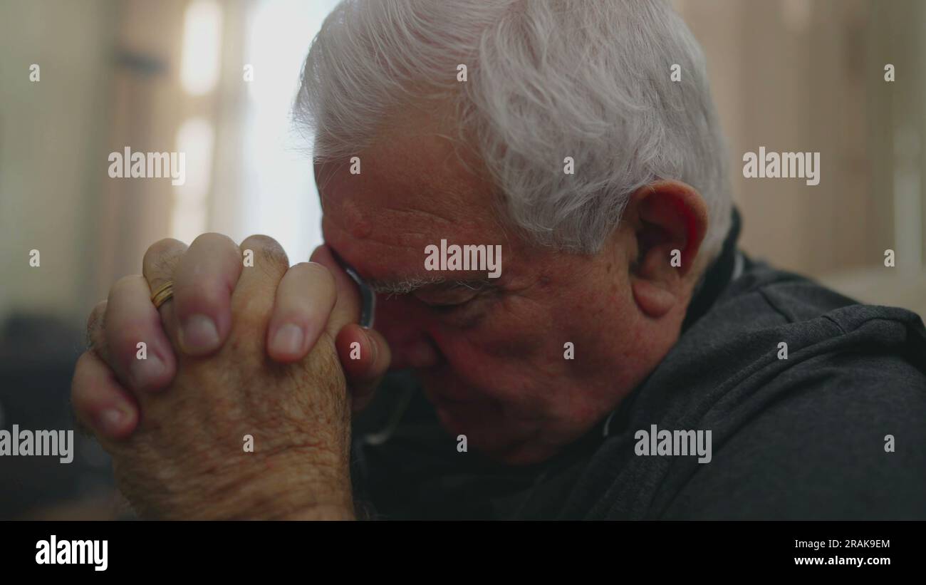 Devoted elderly man PRAYING close-up face with hands clenched together ...