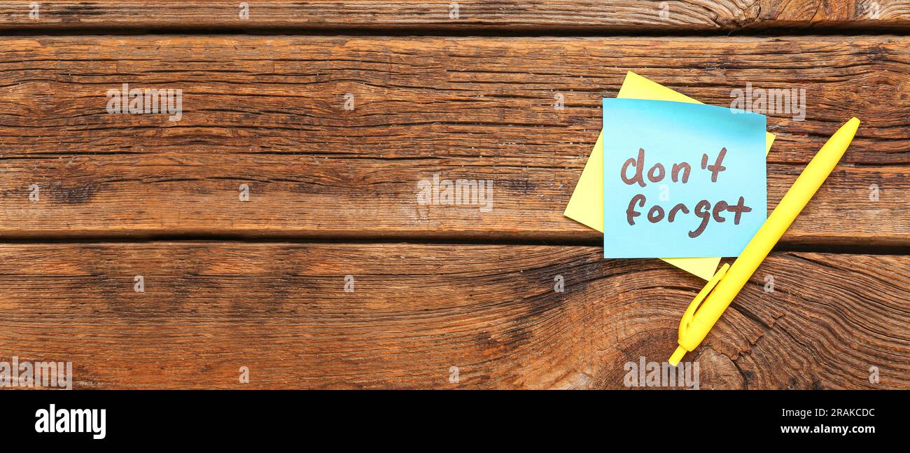 Sticky note with text DON'T FORGET and pen on wooden background with ...