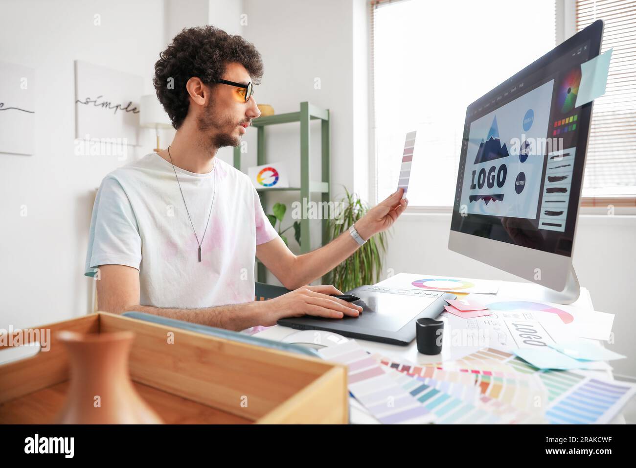 Male graphic designer working with color palette and tablet at table in ...