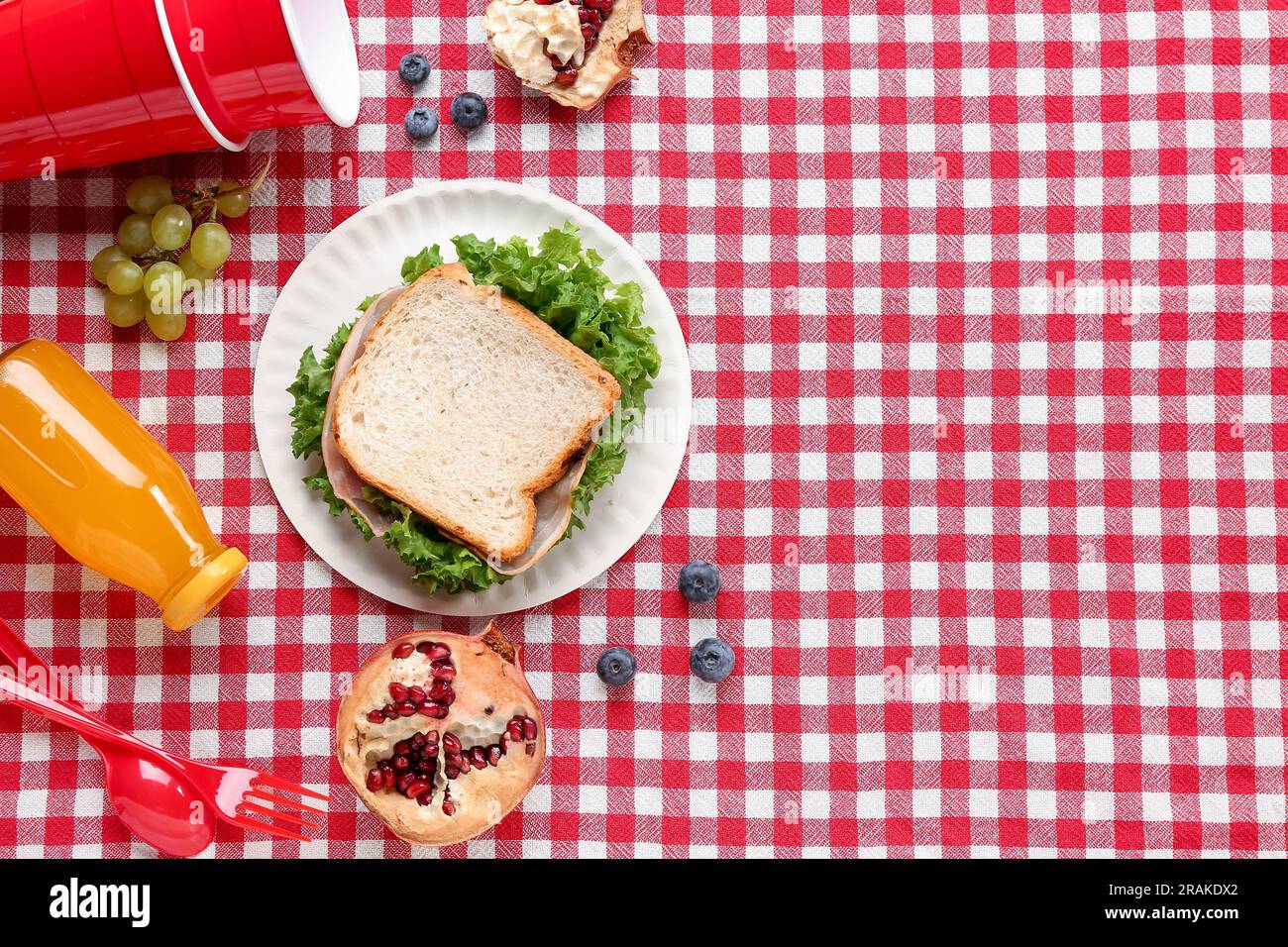 Paper plate with tasty sandwich, juice and plastic tableware on fabric ...