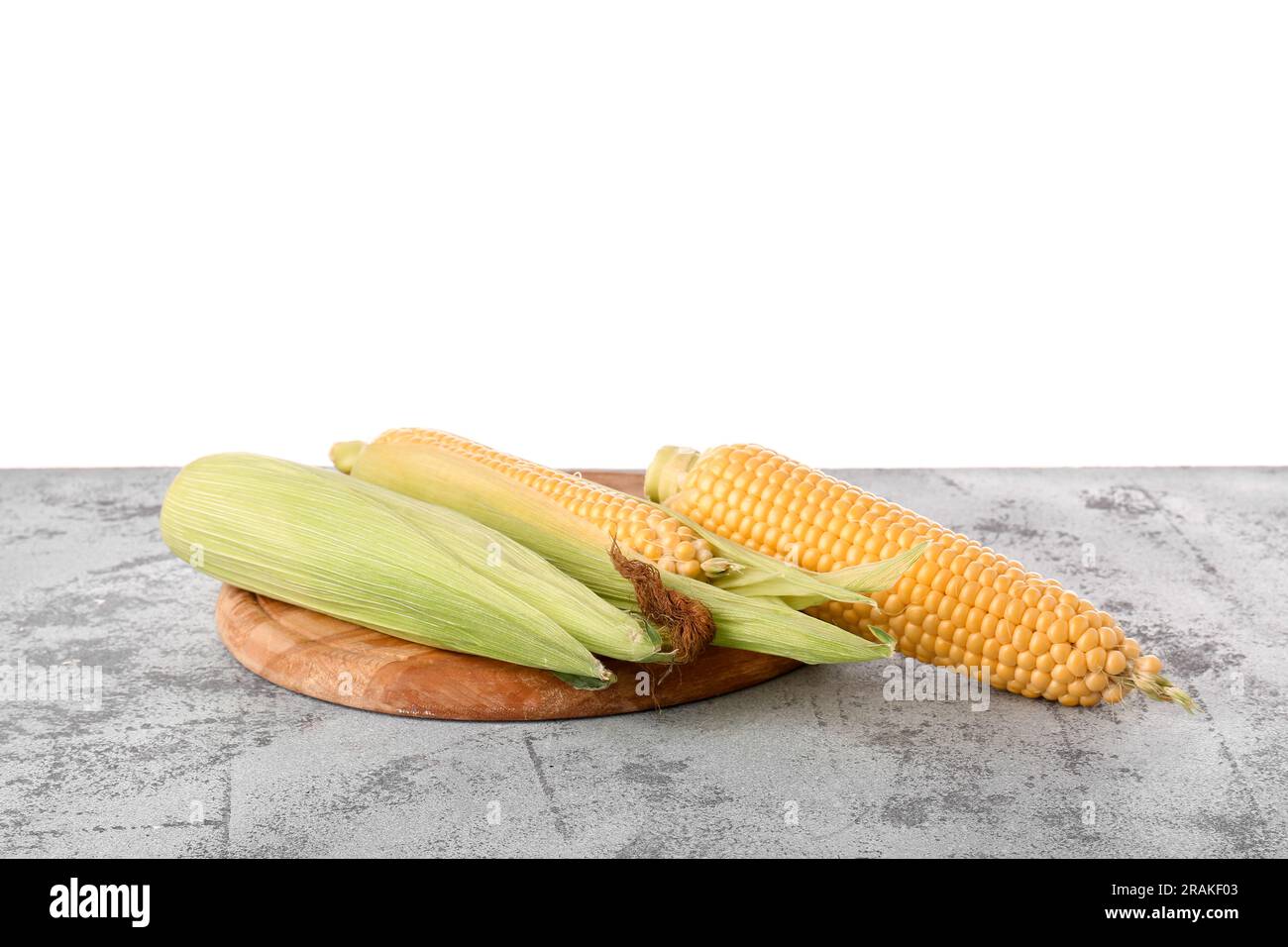 Wooden board with fresh corn cobs on grey table against white ...