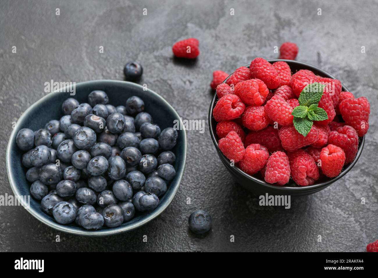 Bowls with fresh raspberry and blueberry on black background, closeup ...