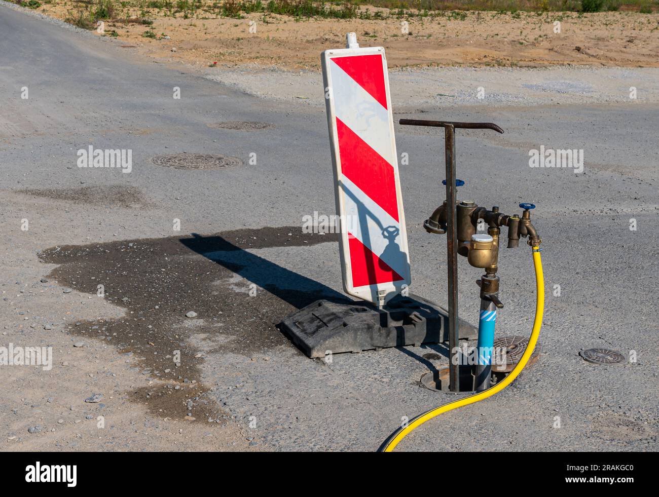 Water hydrant with yellow hose attached and a plastic white-red warning ...