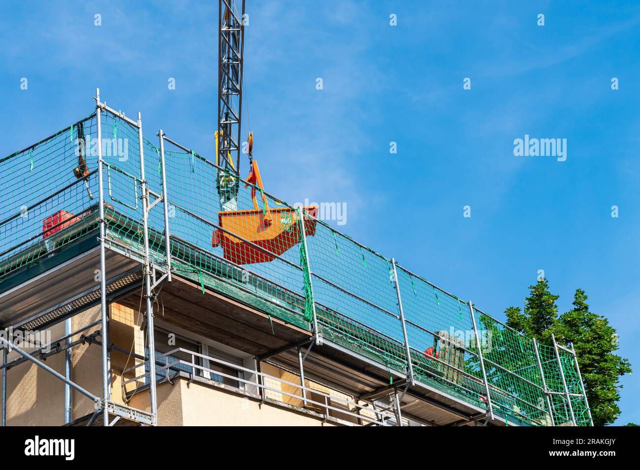 Lifting crane holds an orange container over the roof of a renovated ...