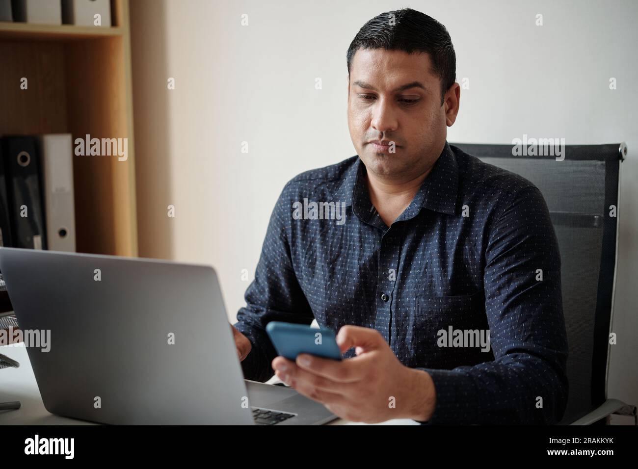 Serious businessman reading text message when working on laptop at ...