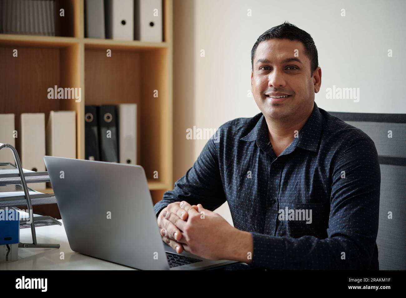 Portrait of cheerful entrepreneur working on laptop at office desk ...