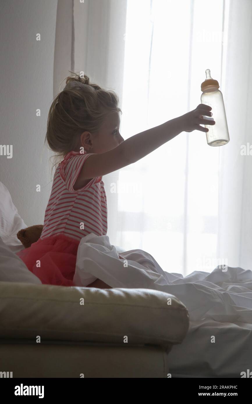 Cute little girl in bed holding plastic baby bottle, concept of ...