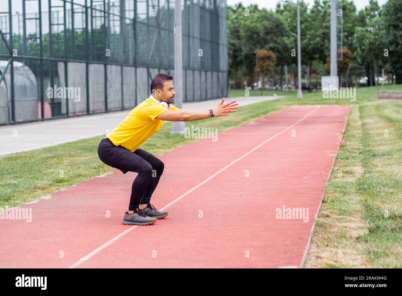 Sportive man in comfortable clothes doing squats with hands reaching ...
