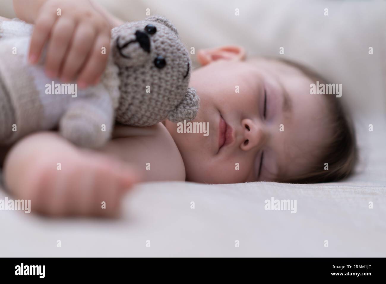 Adorable chubby baby hugging knitted bear toy with hand lying on soft ...
