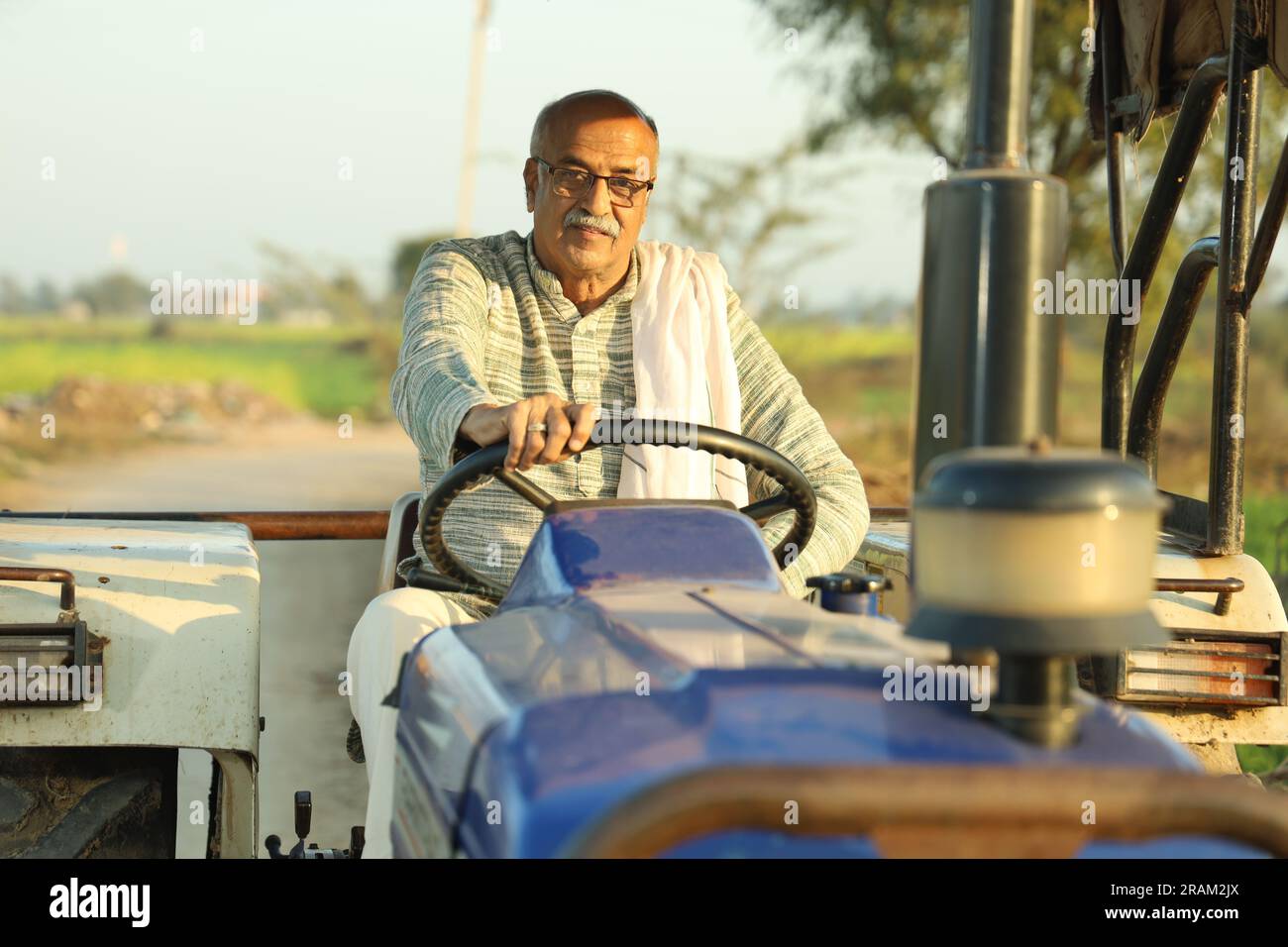Happy hard working Indian farmer sitting on a tractor in a day time ...