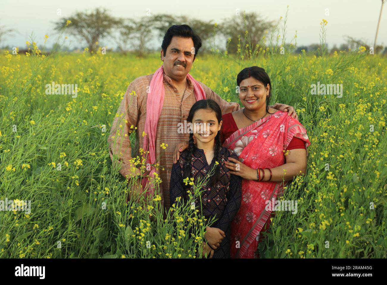 Happy Indian farmers family standing in mustard field in day time ...