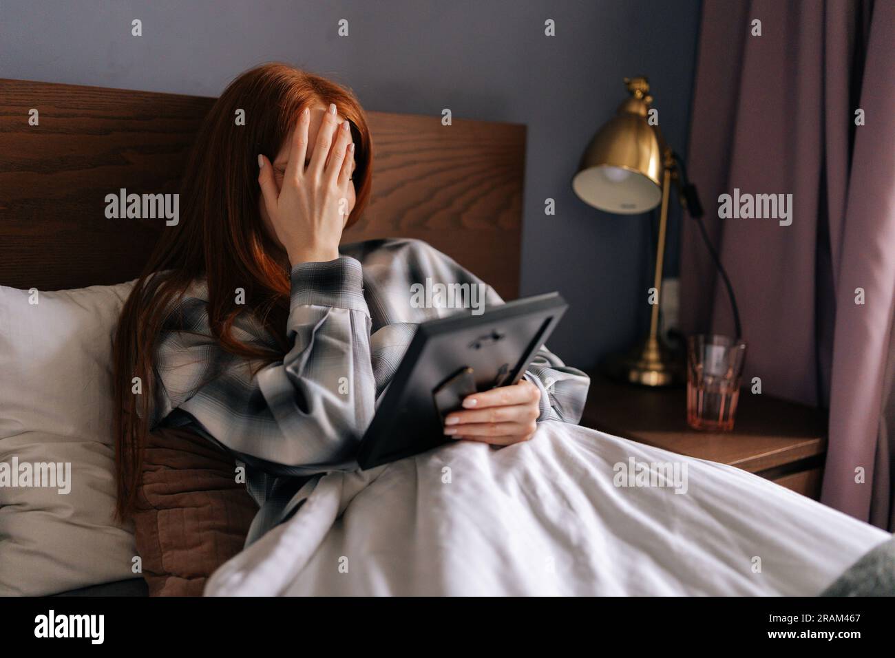 Side view of grief-stricken young woman lying on bed covering face with ...