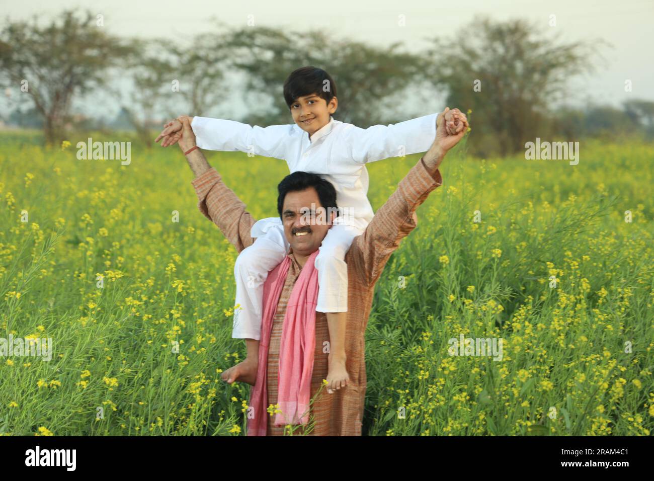 Young happy Indian farmer father standing in mustard field in day time ...