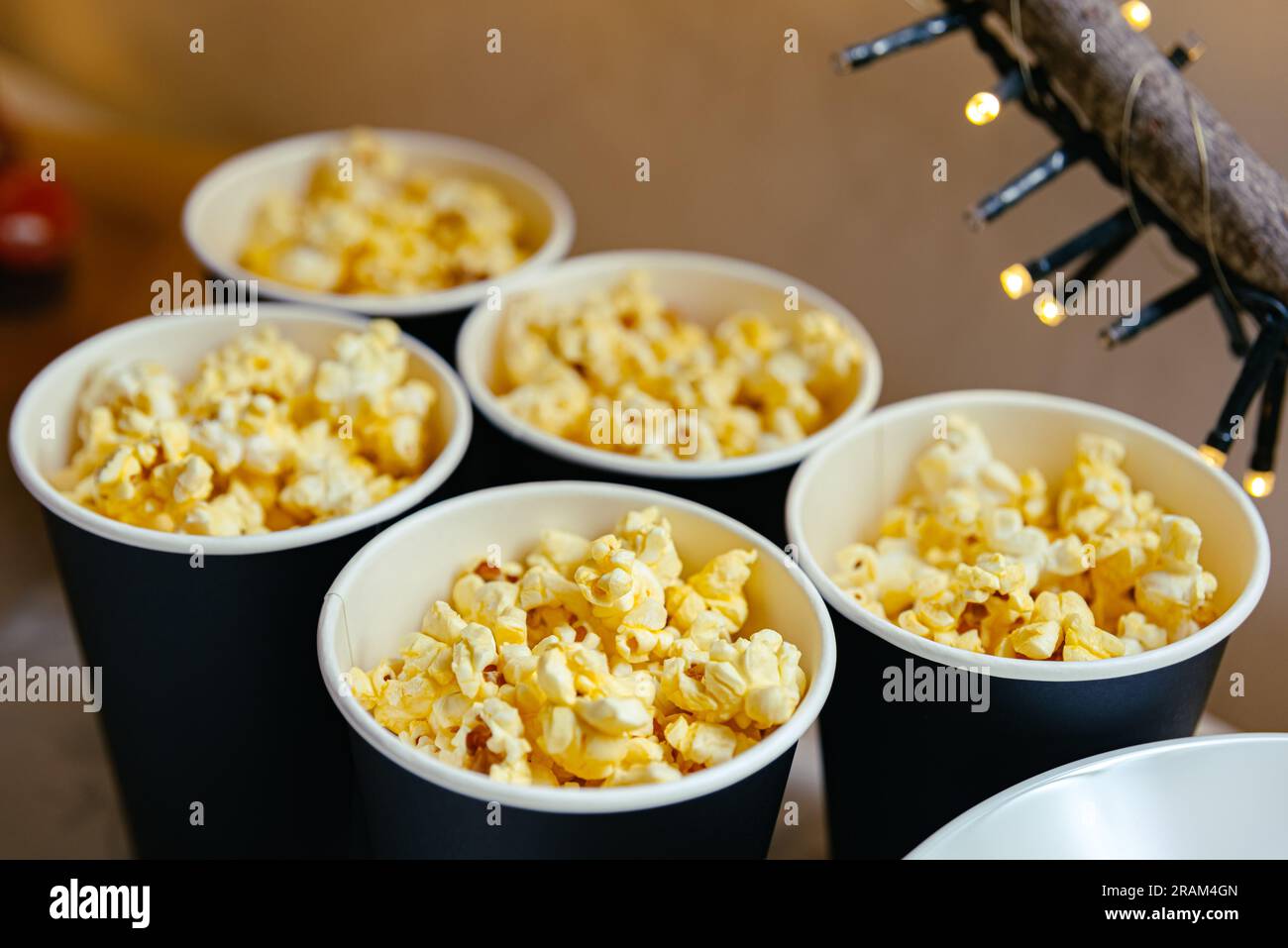 Cheese-flavoured popcorn in paper black cups. A stack of black paper ...