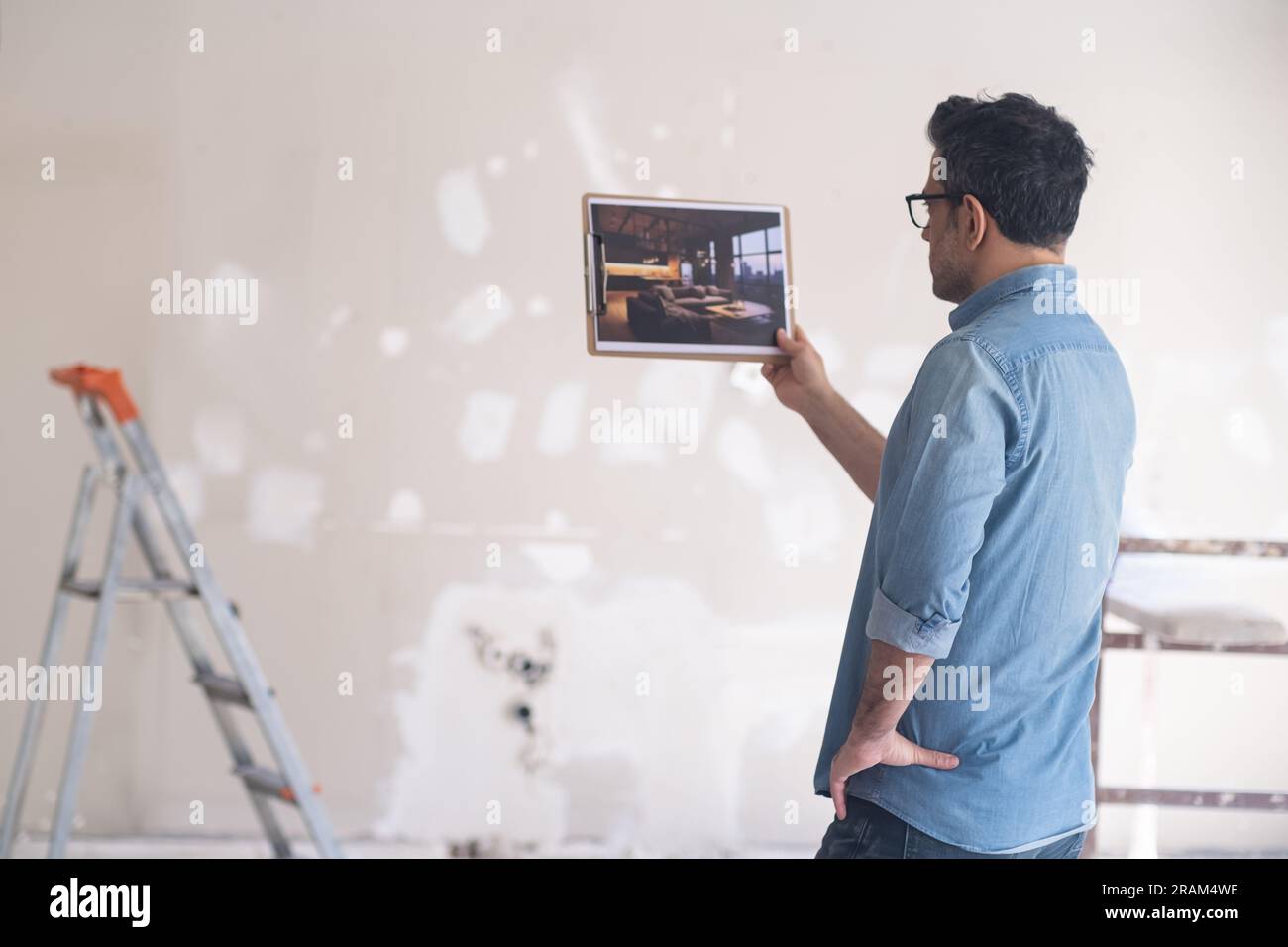 Home owner standing in unfinished premise looks at picture with ...