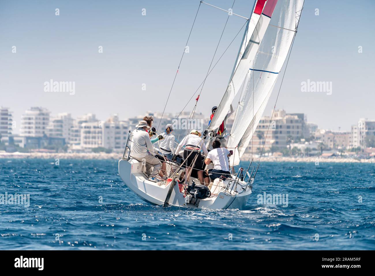 Yacht with crew during regatta in the sea with city on the horizon ...