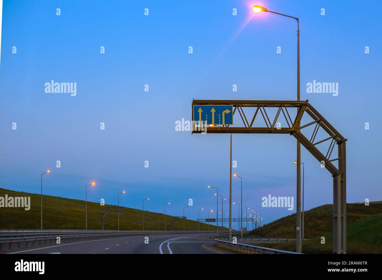 Road with lanterns illuminating the track in the evening. Road sign ...