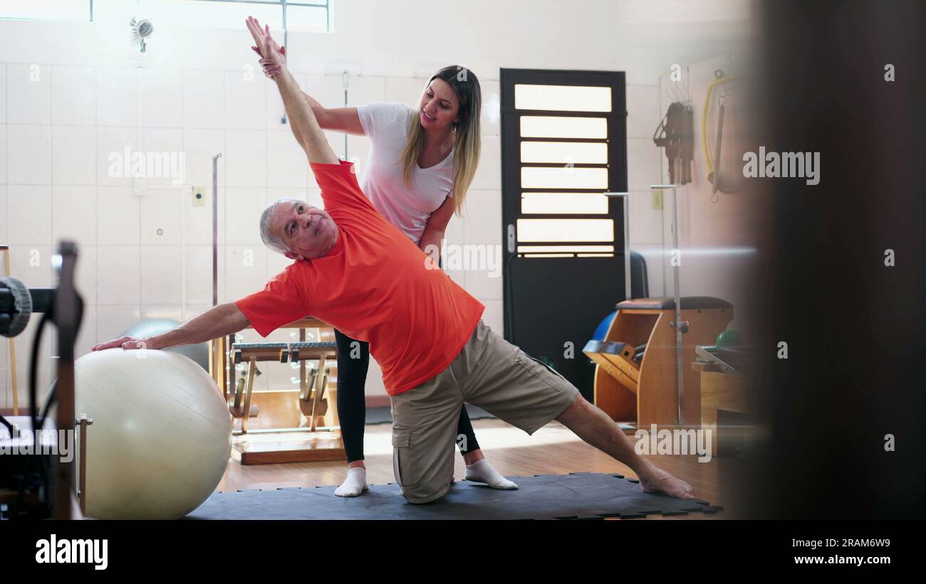 Pilates instructor guiding senior man to exercise with ball. Older ...