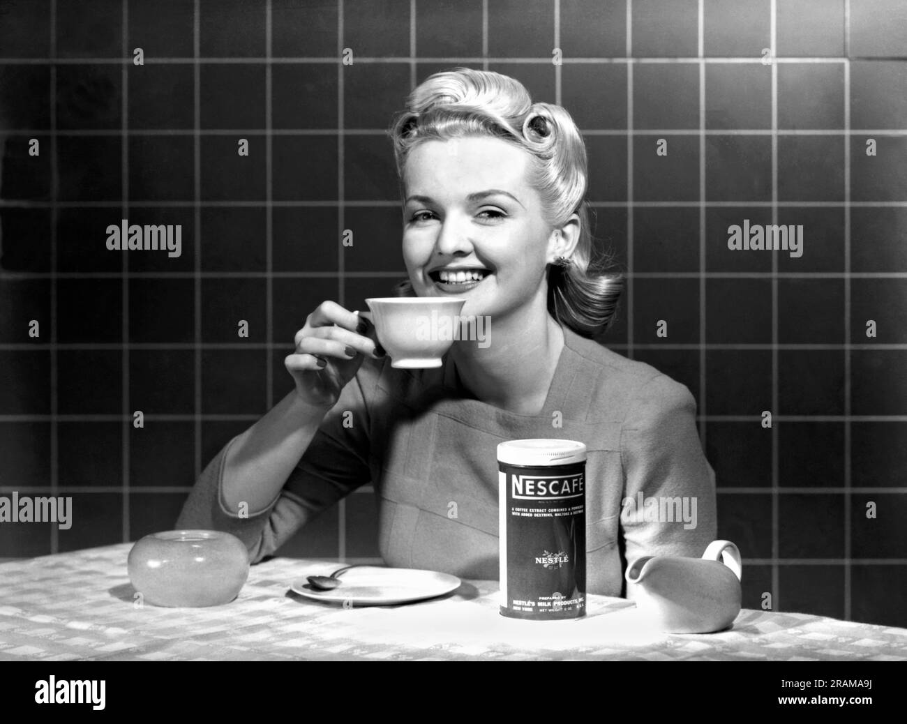 United States: c. 1960. A single woman at a kitchen table enjoys a cup ...