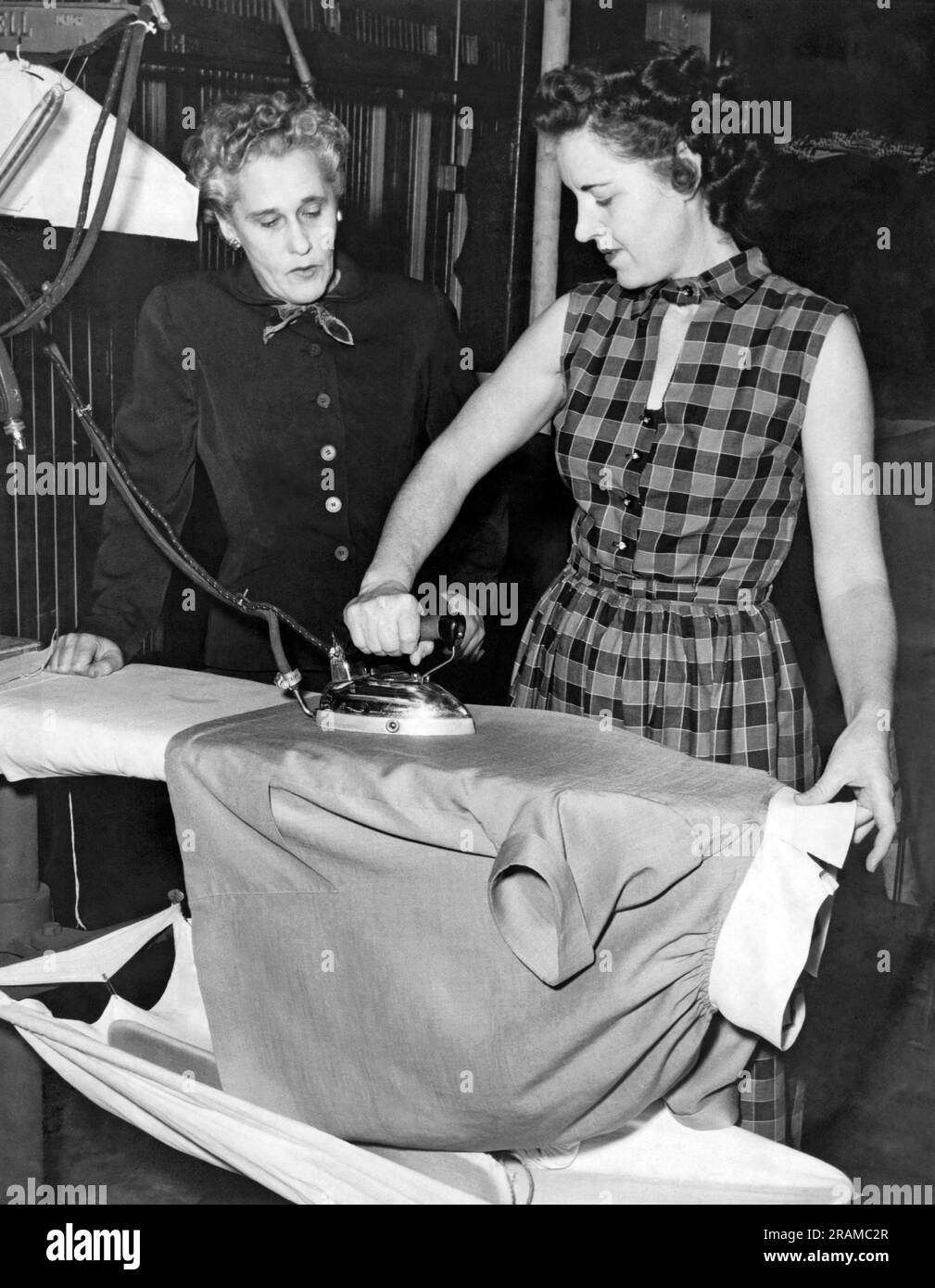 United States: c. 1935. A young woman irons a shirt while an older ...