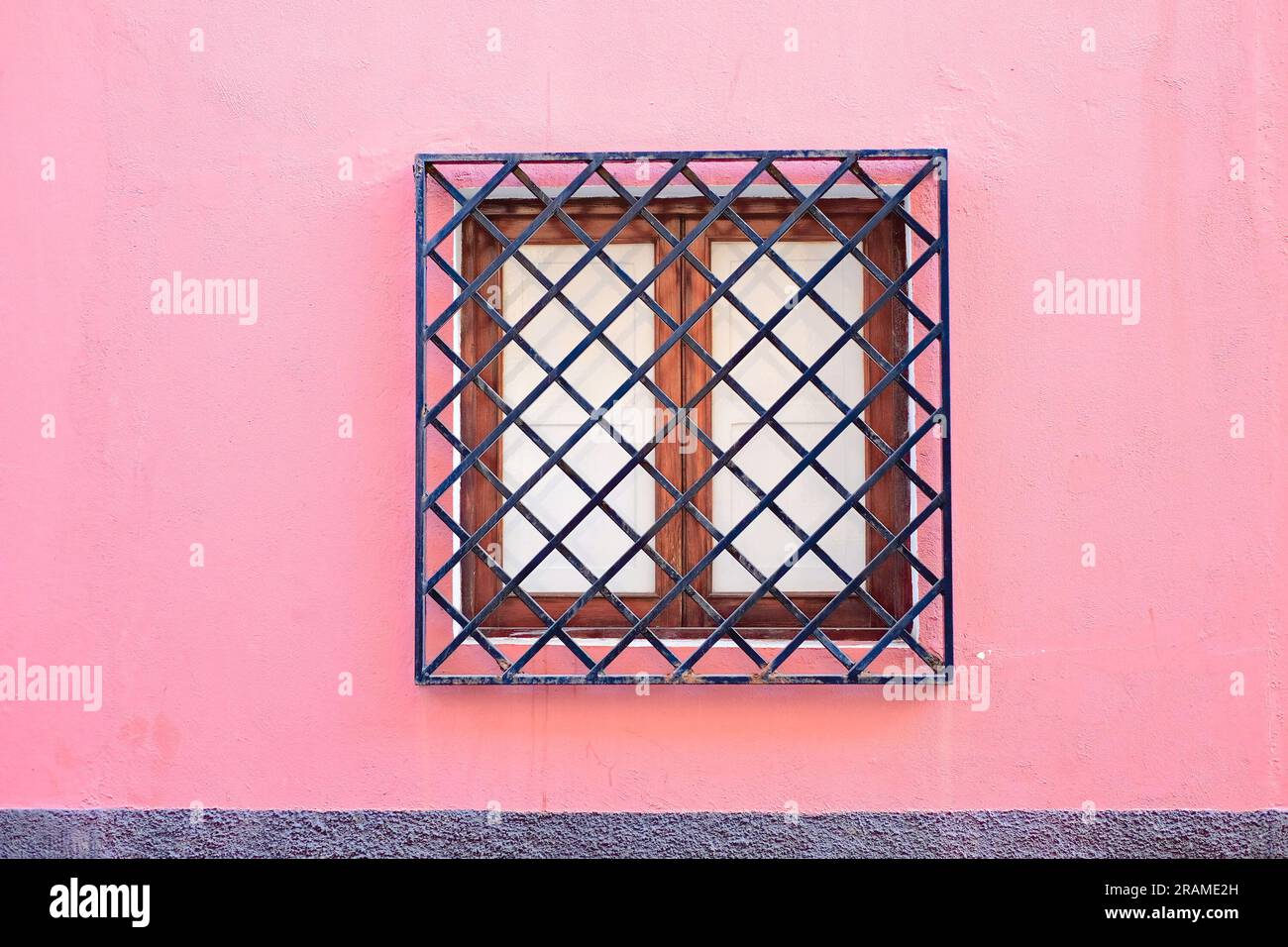 Barred squre window in a pale pink facade of an elegant European villa ...