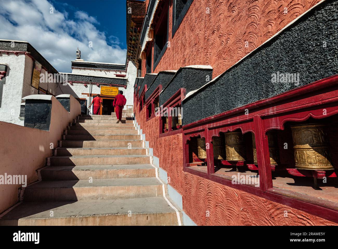 Young Buddhist monks walking on stairs along prayer wheels in Thiksey ...